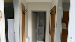 Corredor que dá para um banheiro com chuveiro, um radiador e uma porta com uma toalha pendurada.