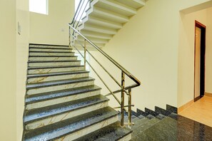 Escadaria com degraus de mármore e corrimãos de metal, levando a um patamar com uma porta.