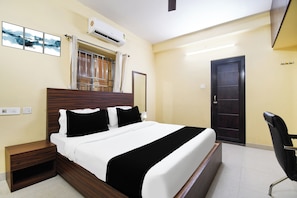 Quarto de hotel com cama, mesa de cabeceira, aparelho de ar condicionado, janela com cortinas e porta.
