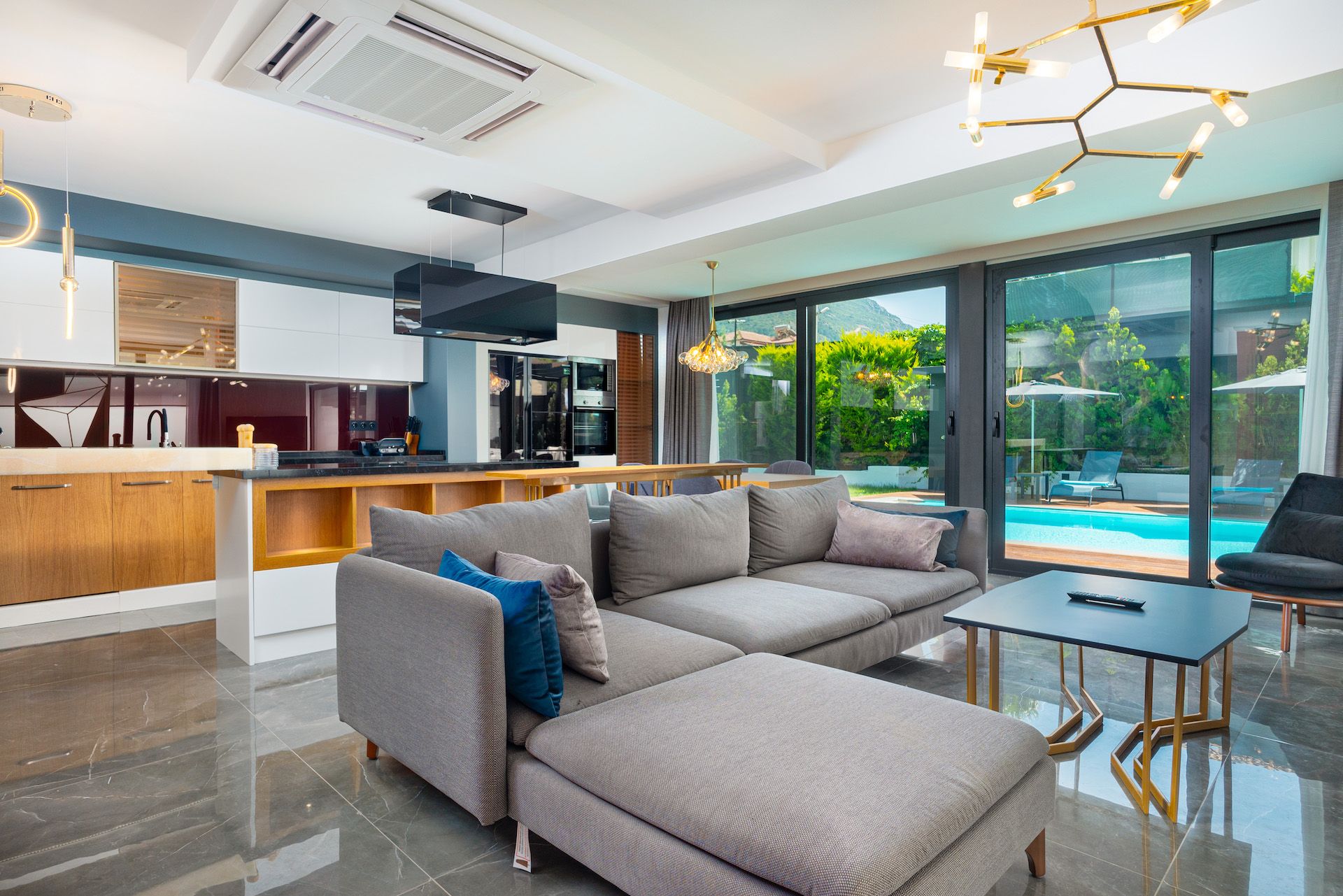 Uma sala de estar moderna com um sofá seccional, uma mesa pequena e vista para uma piscina através de grandes janelas.