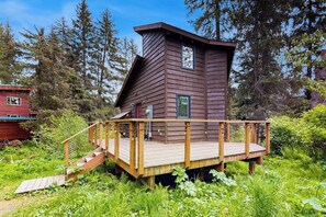 Uma cabana de madeira com varanda, rodeada por vegetação exuberante e árvores.