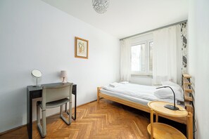 Quarto com cama, escrivaninha, cadeira, mesa de cabeceira, abajur, janela com cortinas e um quadro na parede.