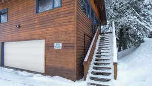 Um edifício de madeira com uma porta de garagem, uma escadaria coberta de neve e um aviso de risco de deslizamento de neve do telhado.