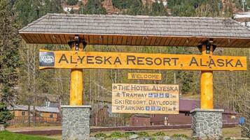 Placa de madeira com 'Alyeska Resort, Alaska' e setas indicando 'The Hotel Alyeska & Tramway' e 'Estância de esqui, Daylodge e estacionamento'.