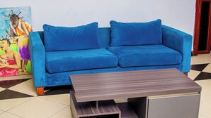Um sofá azul com uma almofada combinando, uma mesa de centro de madeira e um chão de azulejos com padrão quadriculado.