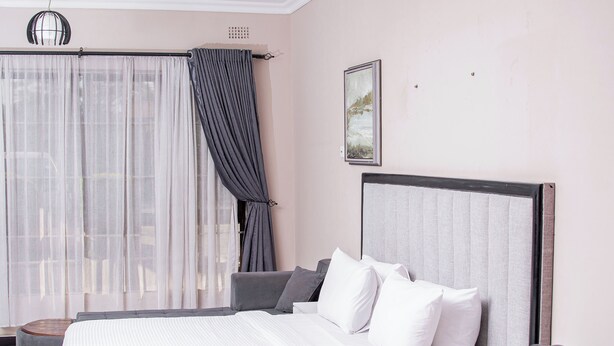 Quarto moderno com cama grande, roupa de cama cinza e branca, sofá cinza e cortinas leves.