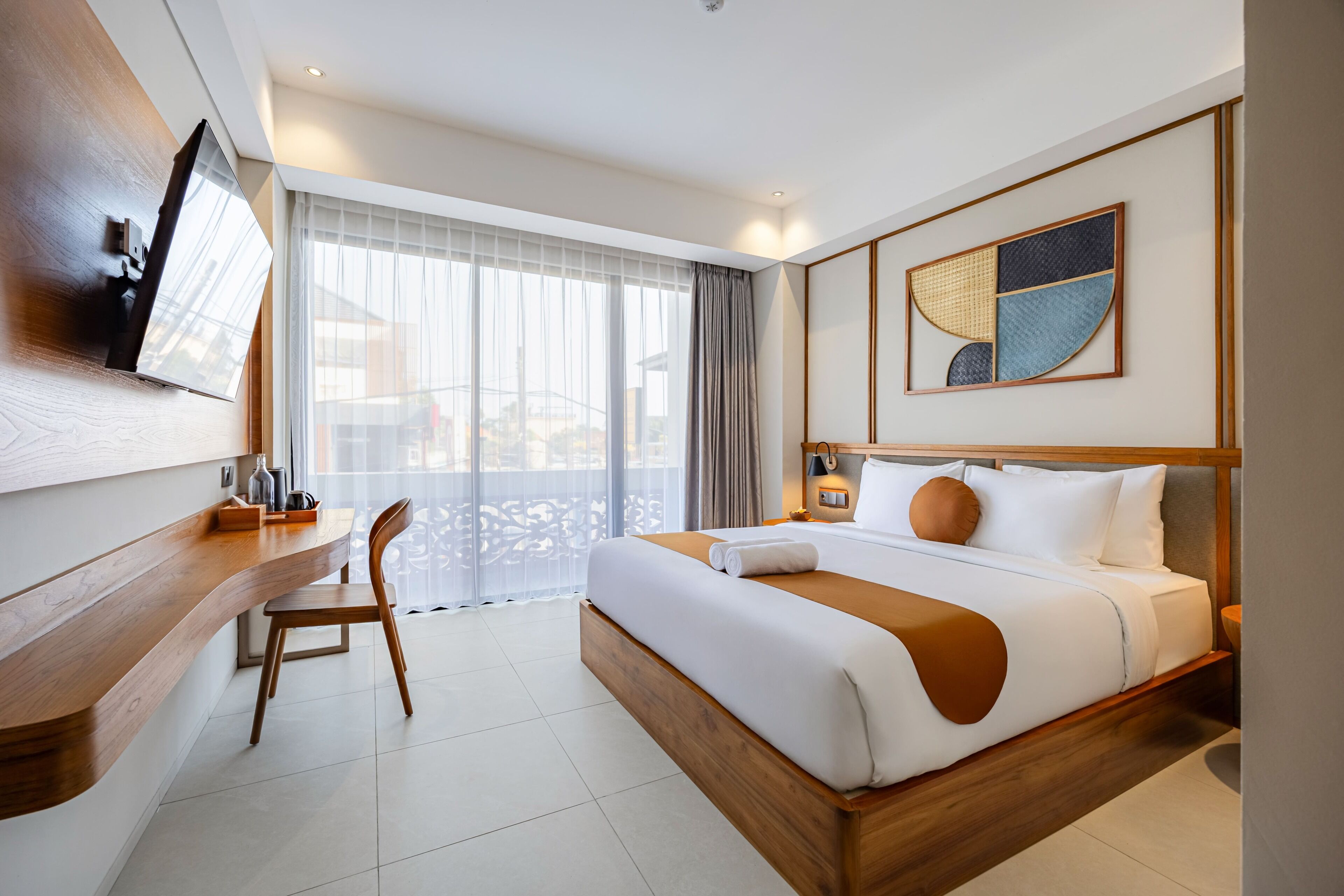 Quarto de hotel moderno com uma cama grande, uma escrivaninha e uma TV fixada na parede.