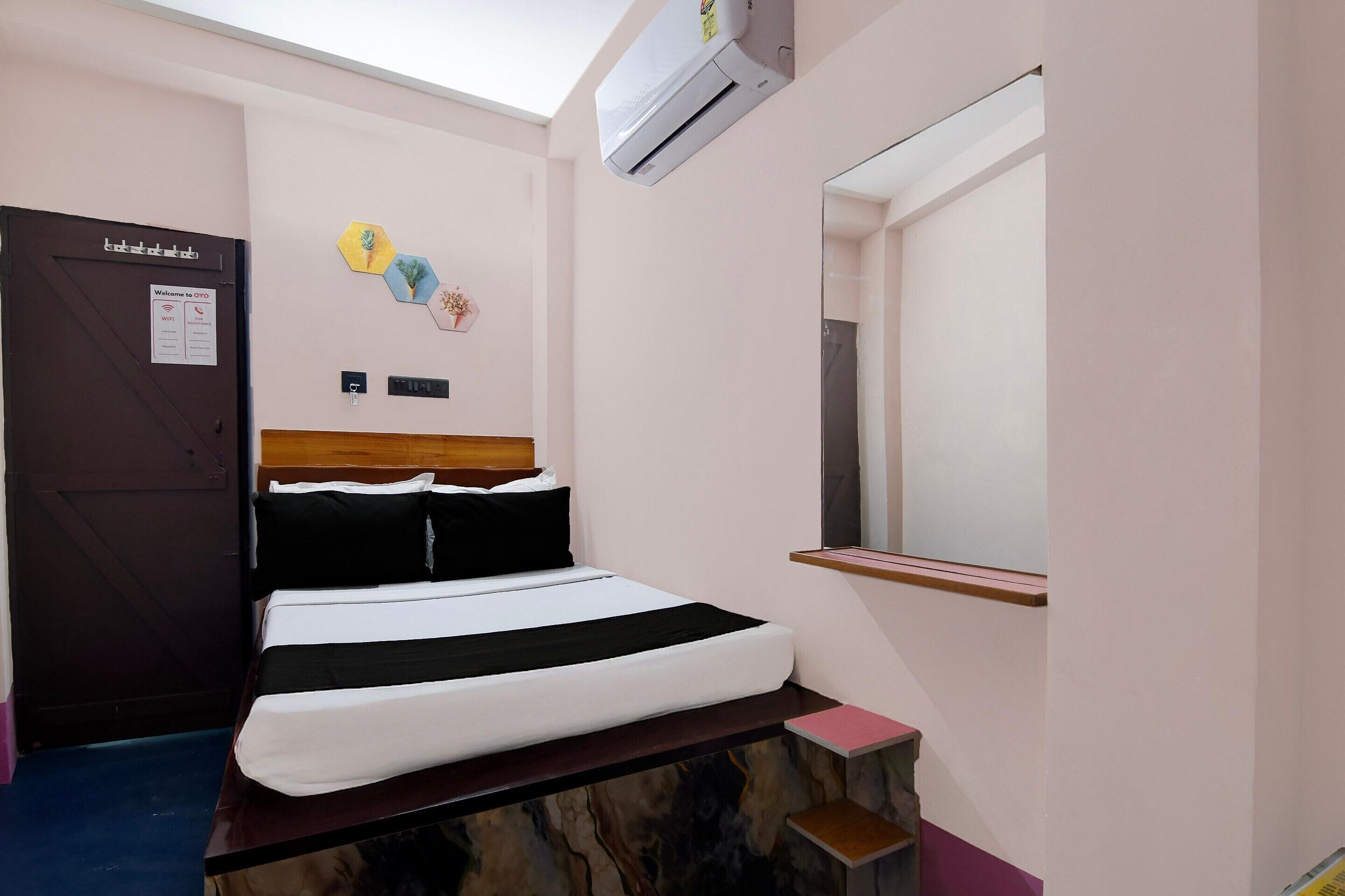 Quarto de hotel com cama, escrivaninha, espelho, ar condicionado e porta com placa.