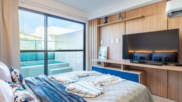 Quarto de hotel com uma cama grande, televisão e varanda com vista para edifícios.