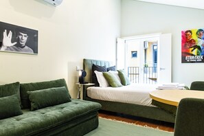 Quarto de hotel moderno com sofá verde, cama com edredom branco, mesa pequena e um pôster de Star Trek na parede.