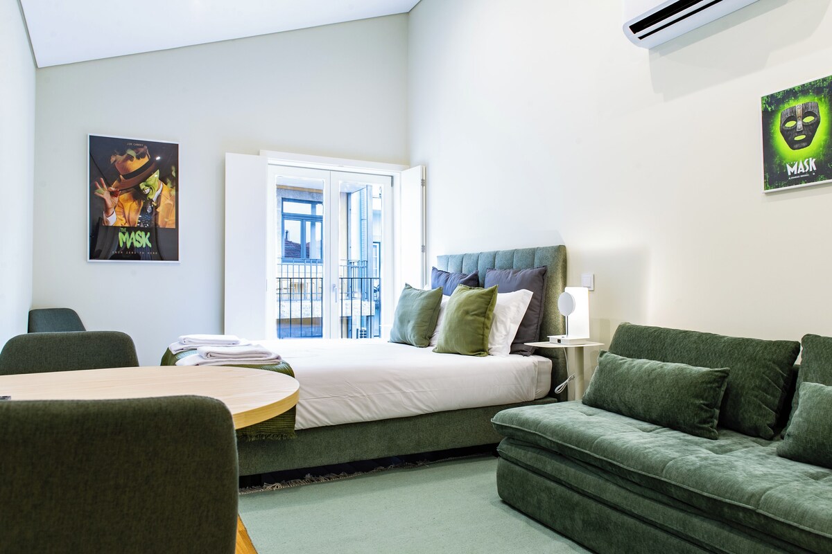 Quarto de hotel com cama, sofá verde, mesa com toalhas e um pôster na parede.