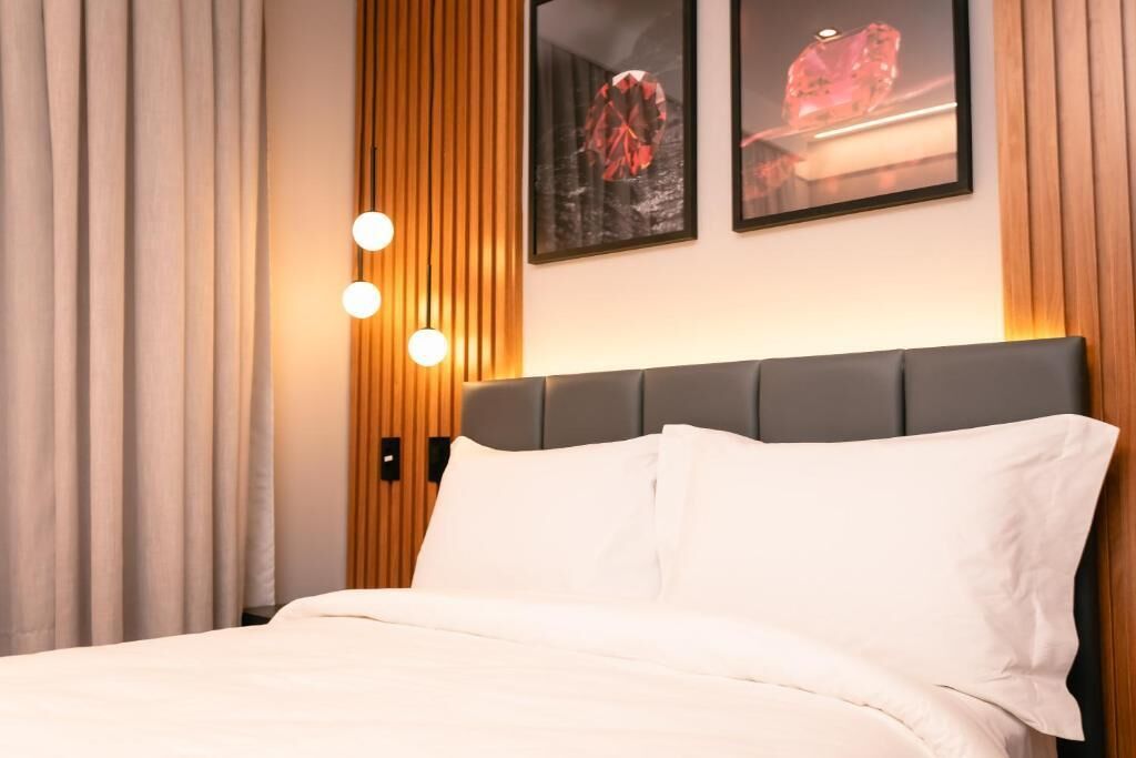 Quarto de hotel com cama, cortinas, luminárias fixadas na parede e obras de arte.