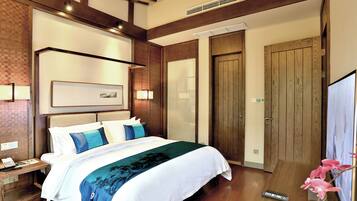 Quarto de hotel com uma cama grande, mesa de cabeceira, televisão na parede e porta de madeira.