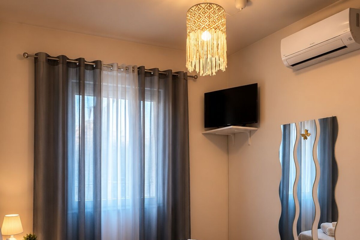 Quarto de hotel com cama, cortinas, televisão e ar condicionado fixado na parede.