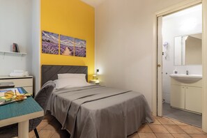 Quarto com cama, mesa de cabeceira, abajur, estante com livros e porta para um banheiro.