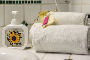 Casa de banho com toalha branca, dispensador de sabão e um objeto decorativo com a forma de uma borboleta sobre a toalha.