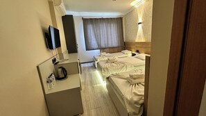 Quarto de hotel com cama, escrivaninha, televisão e janela com cortinas.