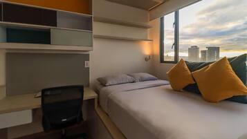Quarto de hotel moderno com uma cama, uma escrivaninha e uma cadeira. Há uma janela com vista para o horizonte da cidade.