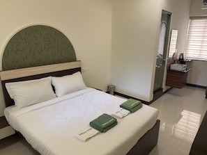 Quarto de hotel com uma cama, mesa de cabeceira, espelho e janela com persianas.