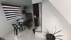 Uma sala de jantar com uma mesa e cadeiras, uma planta em vaso e uma janela com persianas.