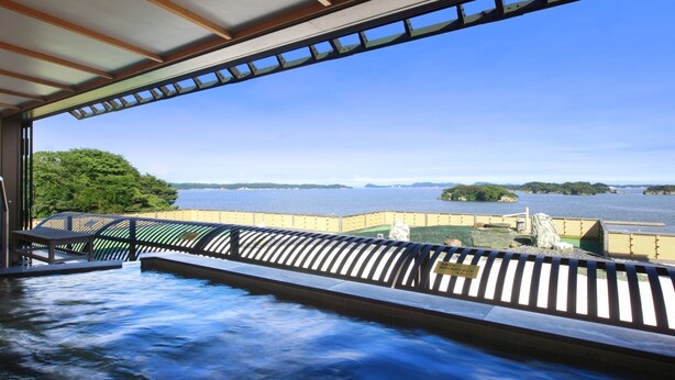 Vista de uma varanda com piscina, dando para um corpo de água e terra ao longe.