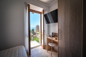 Quarto com cama, escrivaninha e guarda-roupa. Possui varanda com vista para edifícios.