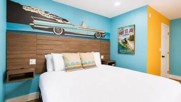 Quarto de hotel com uma cama grande, cabeceira de madeira, um pôster de um cruzeiro e um pôster de um surfista.
