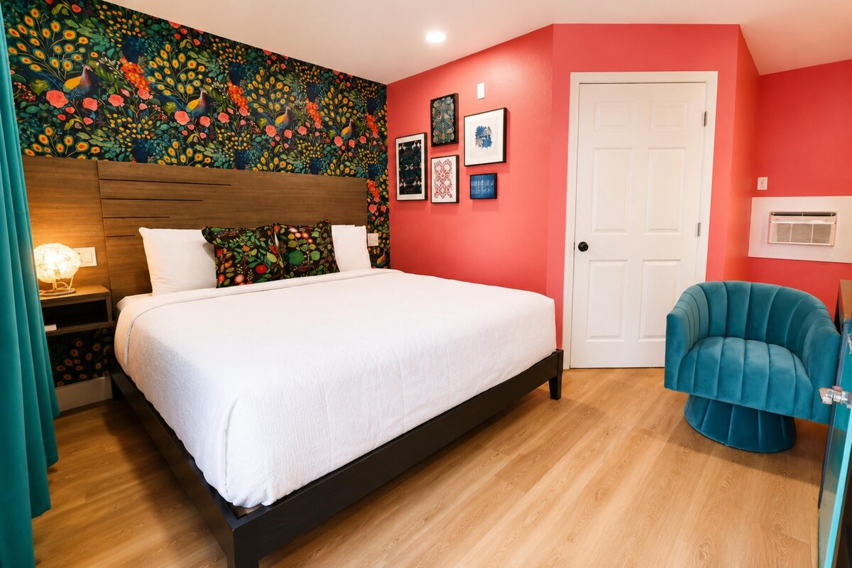 Quarto com cama, cadeira azul, porta e parede com quadros.