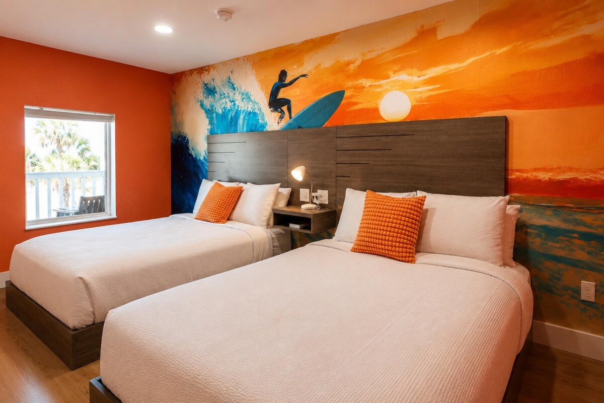 Quarto de hotel com duas camas, uma mesa de cabeceira, um mural na parede e uma janela com vista.
