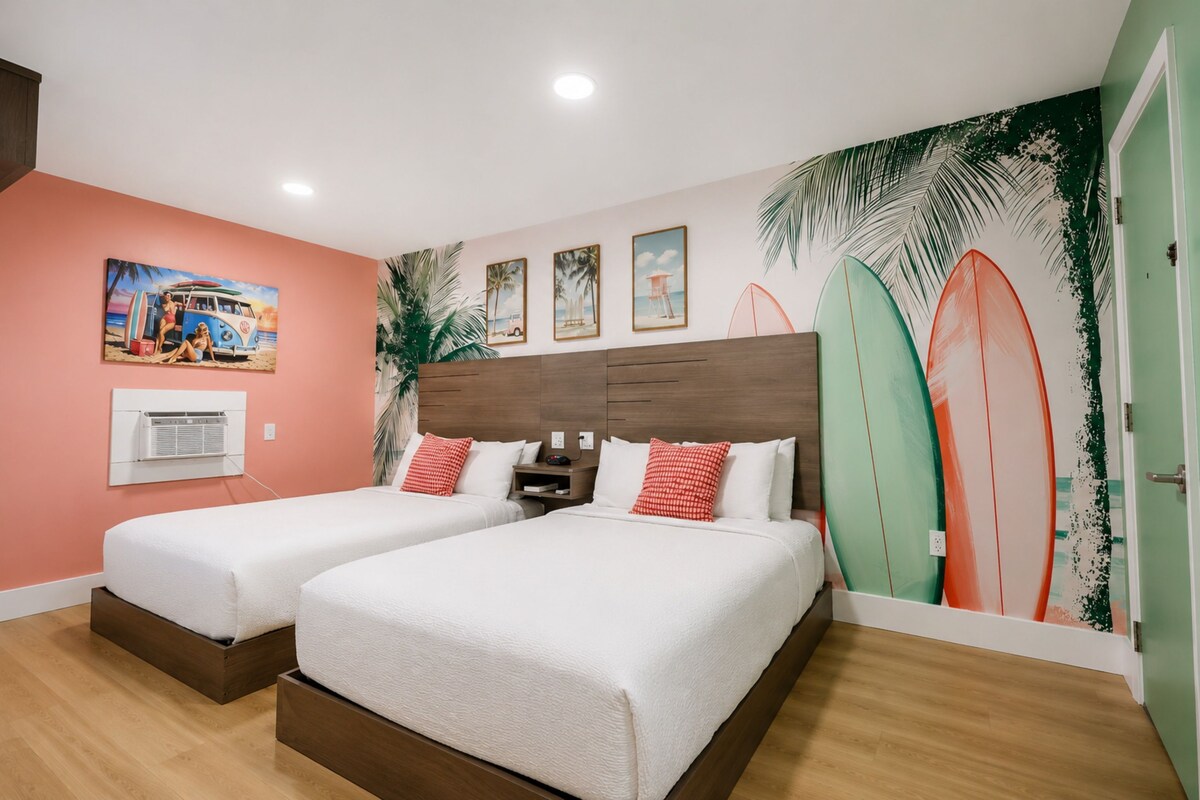 Quarto de hotel com duas camas, um mural temático de praia e uma decoração com prancha de surf.