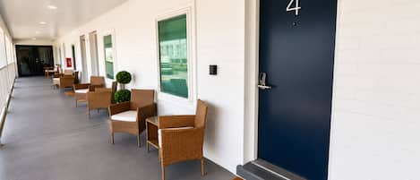 Corredor de hotel com uma fileira de cadeiras de vime e uma porta azul escura identificada com o número 4.