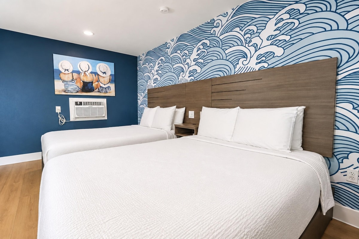 Quarto de hotel com duas camas, cabeceira de madeira e parede com padrão de ondas azuis.