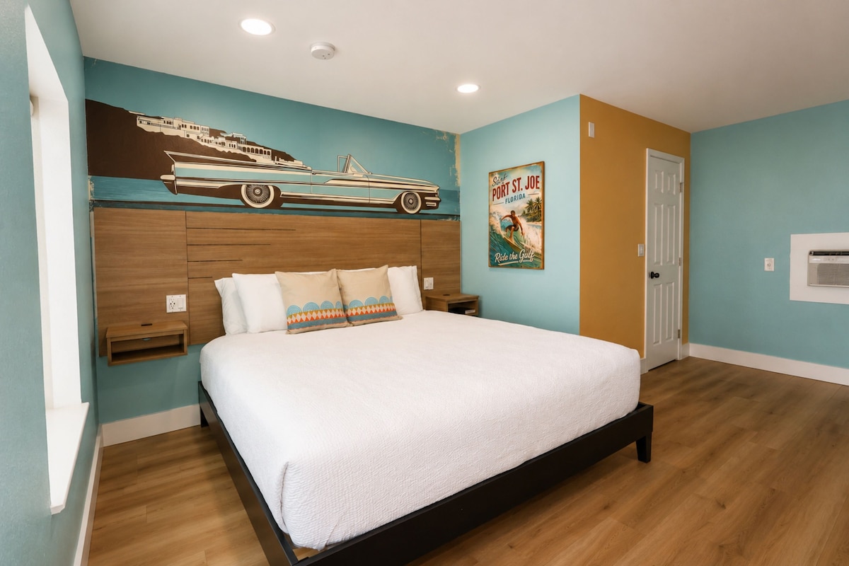Quarto com cama, mesas de cabeceira, cabeceira de madeira, painel na parede, pôster e porta.