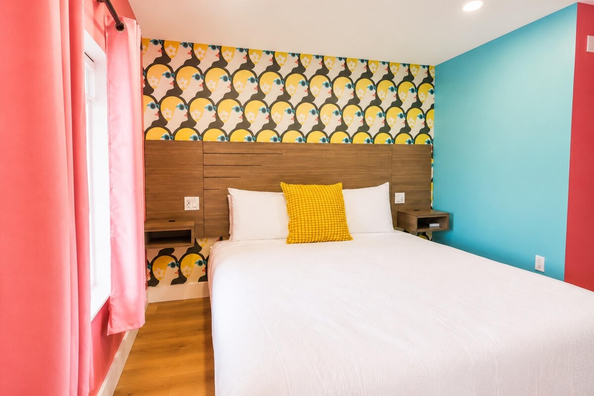 Quarto de hotel com cama, mesa de cabeceira, cabeceira de madeira, papel de parede estampado e parede vermelha.