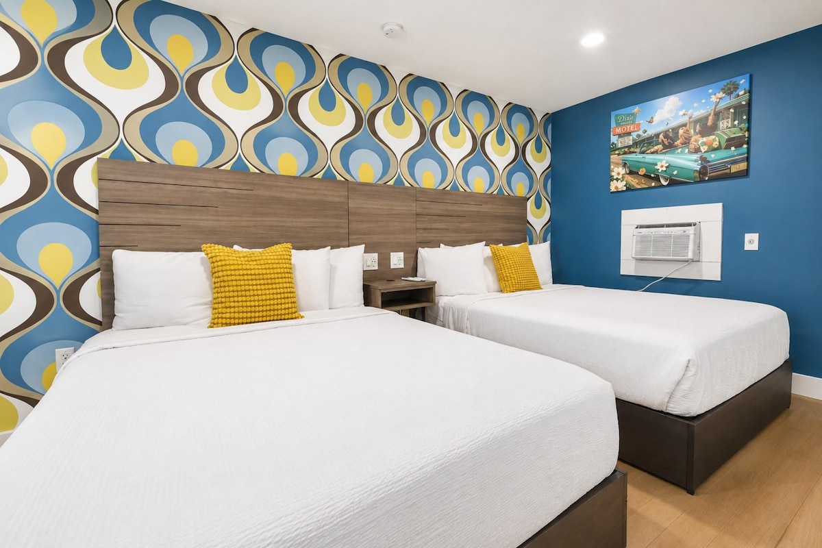 Quarto de hotel com duas camas, parede estampada e um quadro de carro.