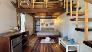Quarto compacto com cama, uma mesinha, escrivaninha e estrutura de teto em madeira.