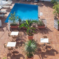 Uma piscina com espreguiçadeiras e mesas, cercada por plantas em vasos e um cercado branco.