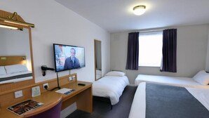 Quarto de hotel com escrivaninha, duas camas de solteiro, televisão e janela com cortinas.