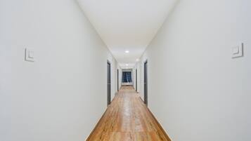 Um corredor comprido e estreito, com paredes brancas e piso de madeira, que leva a uma porta no final.