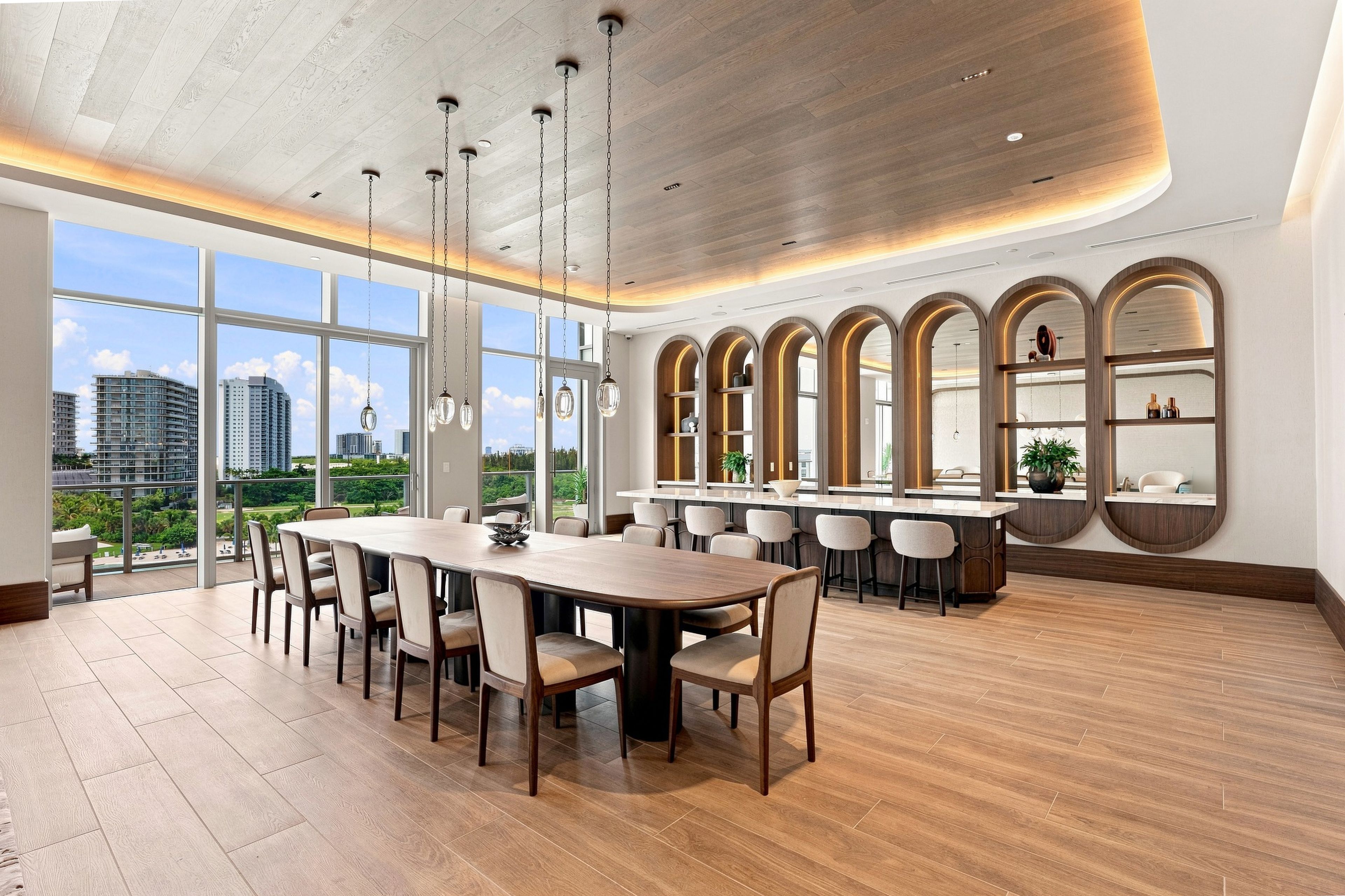 Uma área de refeições moderna com uma grande mesa de madeira e cadeiras, uma cozinha com bancada e grandes janelas com vista para a cidade.