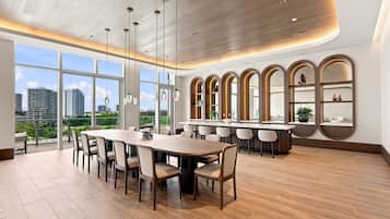 Uma área de refeições moderna com uma grande mesa de madeira e cadeiras, uma cozinha com bancada e grandes janelas com vista para a cidade.