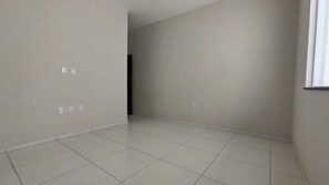 Quarto com soalho em azulejos e paredes lisas, apresentando uma porta e um interruptor na parede.