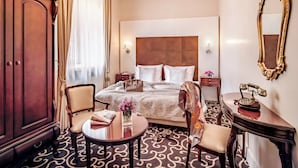 Quarto de hotel com uma cama grande, um guarda-roupa de madeira, uma mesa redonda e um telefone antigo.