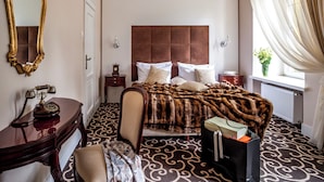 Quarto de hotel com uma cama grande, um telefone antigo, um espelho e uma janela com cortinas.