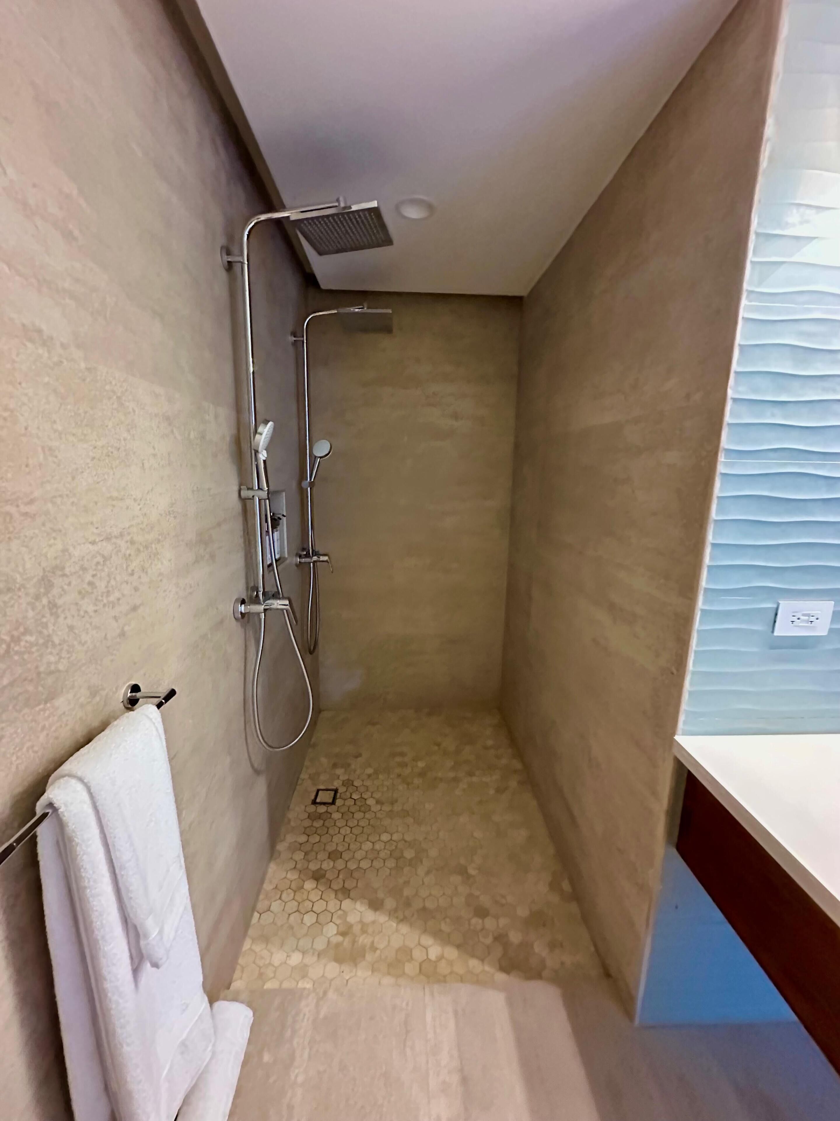 Um chuveiro pequeno e revestido com azulejos, com um chuveiro manual e um painel de controle fixado na parede.