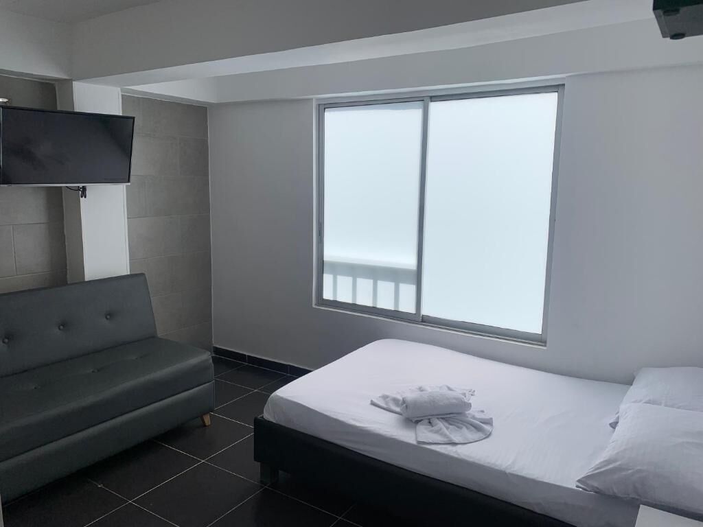 Quarto de hotel moderno com cama, sofá, televisão de tela plana e uma janela grande.