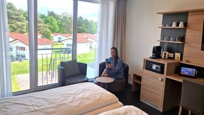 Quarto de hotel com uma cama, uma cadeira, uma escrivaninha, uma máquina de café e uma televisão.