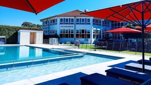 Uma piscina com espreguiçadeiras e guarda-sóis, um edifício com endereço de site, e uma área cercada.