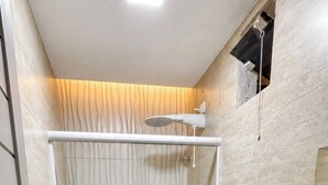 Casa de banho compacta com chuveiro em cabine de vidro, sanita, lavatório e suporte para toalhas.