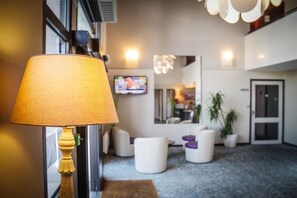 Um saguão de hotel com luminária, área de estar, televisão e uma porta.